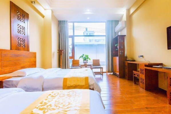 Quarto de hotel com duas camas, uma escrivaninha, uma cadeira e vista para o exterior.
