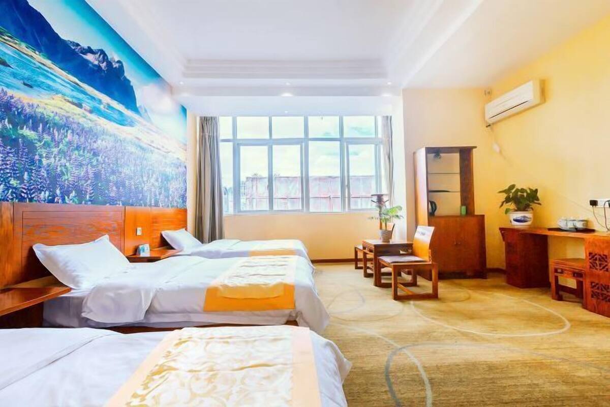 Quarto de hotel com três camas, uma janela grande, um quadro na parede e um armário de madeira.