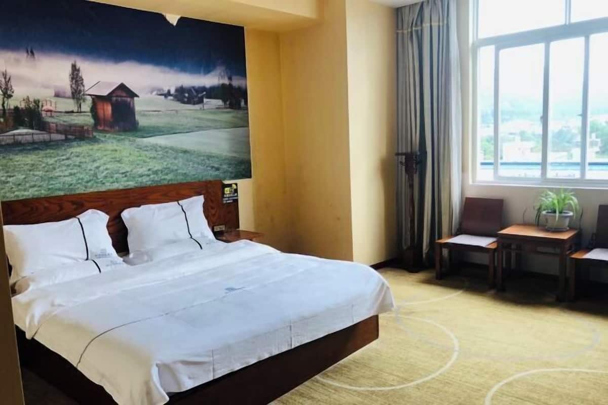Quarto de hotel com uma cama grande, uma escrivaninha, uma cadeira, uma janela com cortinas e um quadro na parede.
