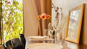 Mesa posta com pratos, talheres e copos, com um vaso de flores e um quadro na parede.
