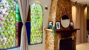 Um quarto com lareira de pedra, uma janela grande com cortina e uma parede de pedra.