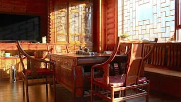 Interior em madeira com uma mesa de jantar e cadeiras, uma janela com persianas estampadas e um banco.