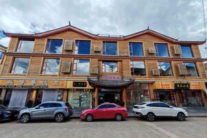 Um edifício de vários andares com estilo arquitetônico tradicional, destacando uma entrada central com toldo decorativo. Vários carros estão estacionados na frente, e o edifício possui diversas placas indicando diferentes estabelecimentos ou serviços.
