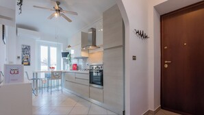 Cozinha moderna com forno embutido, espaço de refeições com mesa e cadeiras, e uma grande porta de madeira.
