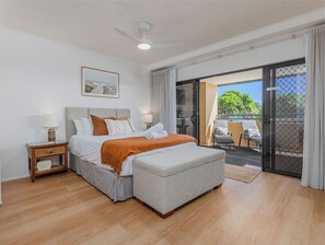 Quarto com cama, mesa de cabeceira, luminária e vista para a varanda.