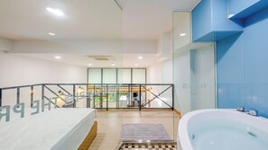 Quarto de hotel moderno com uma banheira grande, varanda envidraçada e escada para área externa.