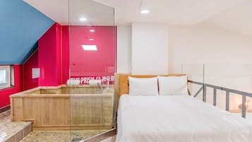 Quarto de hotel moderno com banheira de madeira, cama com roupa de cama branca e parede de destaque vermelha.