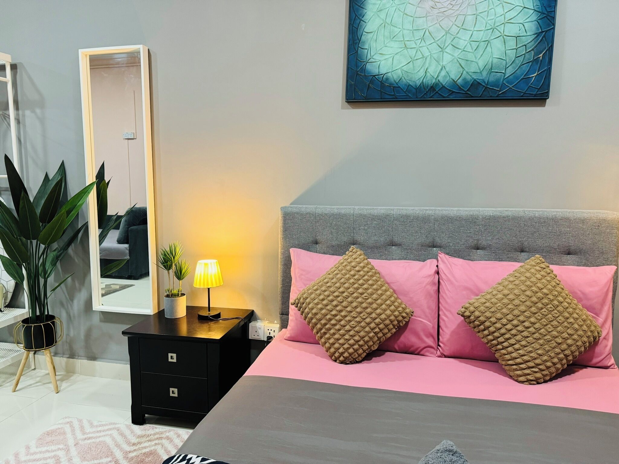 Quarto com cama, mesa de cabeceira, abajur e um espelho grande.