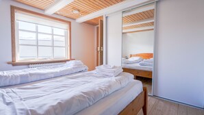 Quarto com duas camas, uma janela grande e uma porta deslizante para outro cômodo.