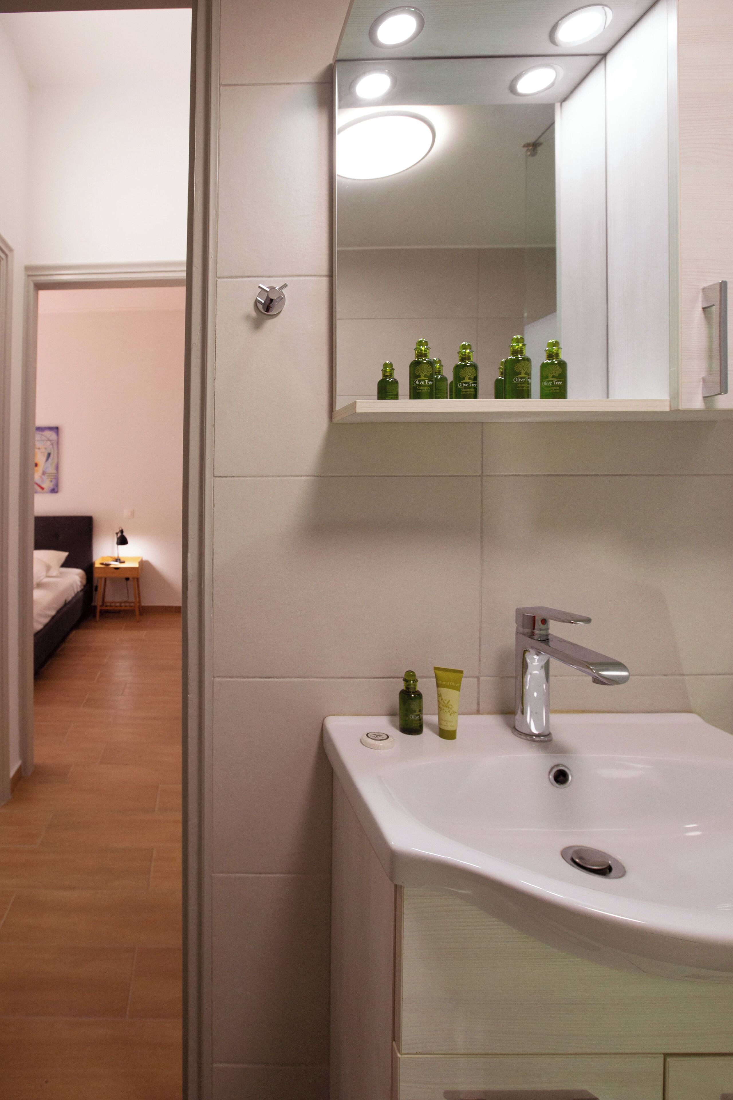 Casa de banho com lavatório branco, espelho e prateleira com produtos de higiene pessoal.