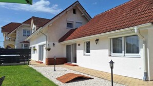 Uma casa de dois andares com telhado de telhas vermelhas, paredes externas brancas e um pequeno alpendre frontal com degraus.