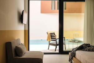 Quarto de hotel com sofá, cama, vista para uma piscina e uma cadeira do lado de fora.