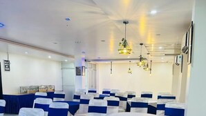 Uma sala de banquetes com fileiras de mesas e cadeiras, cada uma com toalhas e capas azuis e brancas.
