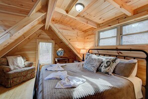 Quarto de sótão acolhedor com cama, sofá floral e janela com vista para uma floresta.