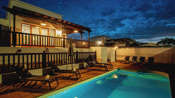 Uma casa moderna com dois andares, piscina, área de estar externa e um terraço coberto.