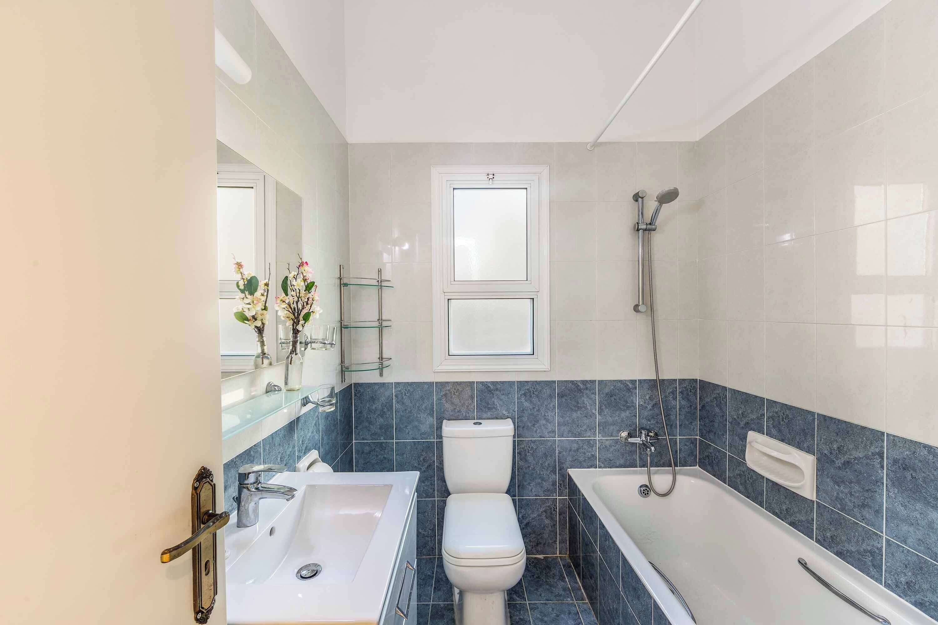 Uma casa de banho com lavatório branco, sanita e banheira, com azulejos azuis e brancos.