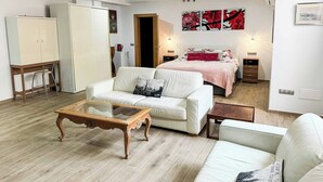 Quarto de hotel moderno com sofá branco, mesa de centro de vidro, cama com colcha rosa e guarda-roupa.