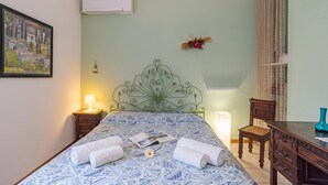 A neatly made bed with a patterned bedspread, a decorative wall hanging, a framed picture, and a small table with a lamp.