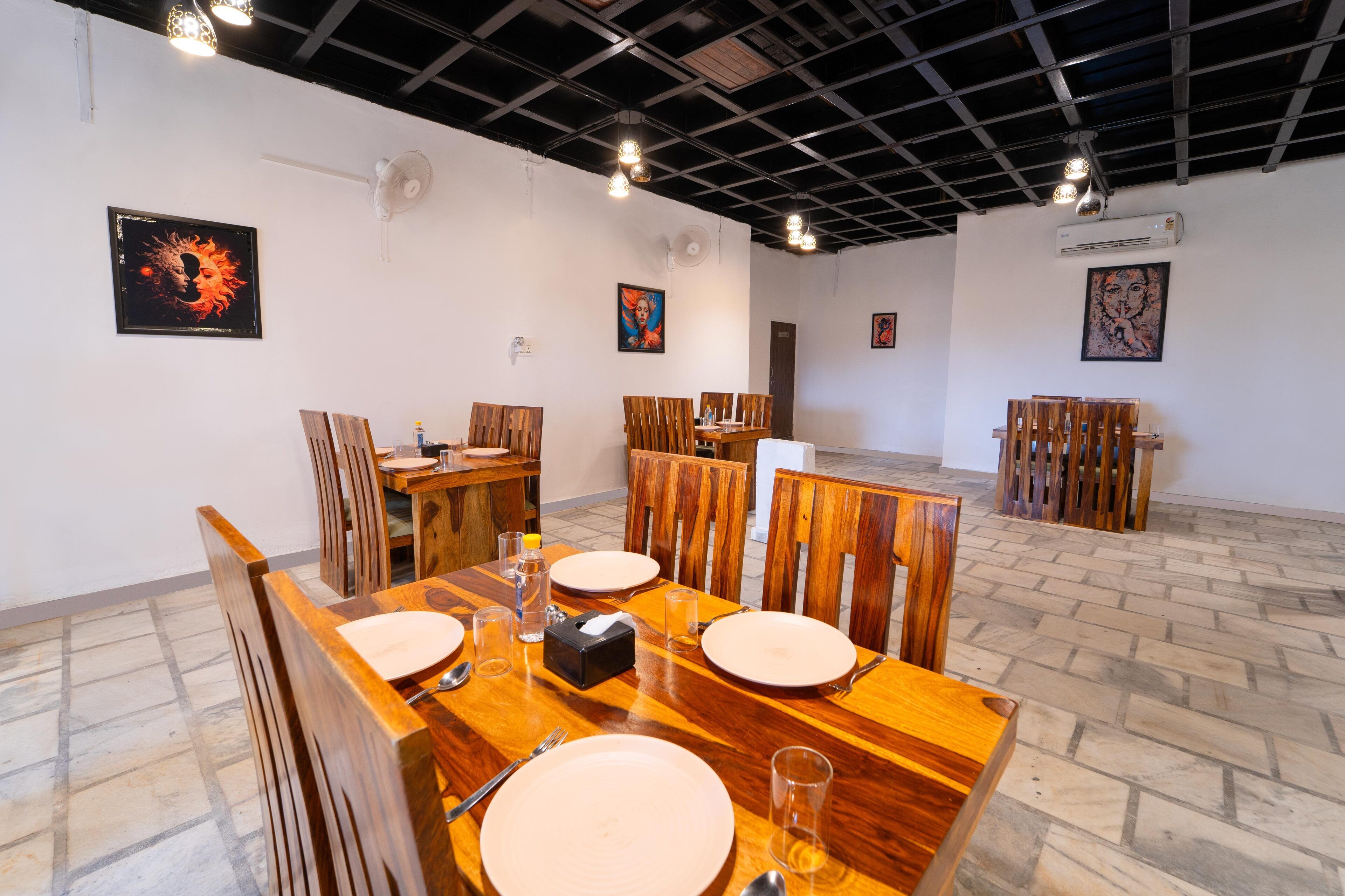 Uma área de jantar com mesas e cadeiras de madeira, um ventilador de teto e obras de arte nas paredes.