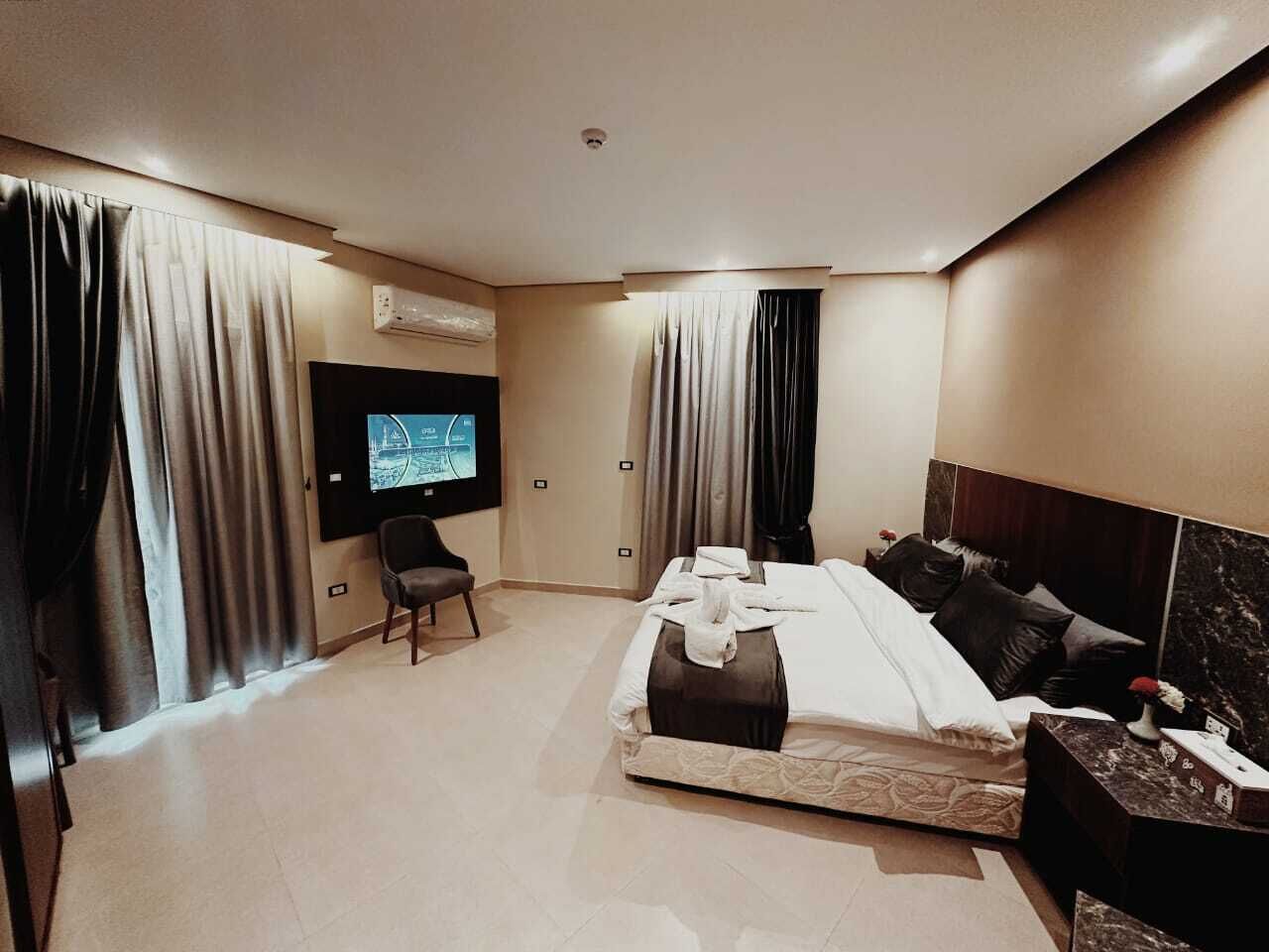 Quarto de hotel moderno com uma cama grande, uma televisão fixada na parede e uma escrivaninha com uma cadeira.