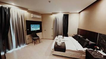 Quarto de hotel moderno com uma cama grande, uma televisão fixada na parede e uma escrivaninha com uma cadeira.