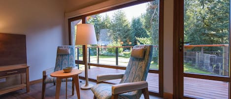 Quarto com duas poltronas, uma mesa pequena e um abajur. Há uma janela grande que oferece vista para o exterior.