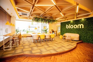 Um interior moderno com piso em padrão herringbone de madeira, parede verde com a palavra "bloom" e uma área de estar com cadeiras amarelas.