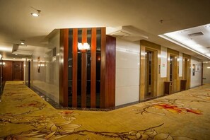 Corredor de hotel com carpete estampado, painéis de madeira e portas que dão para os quartos.
