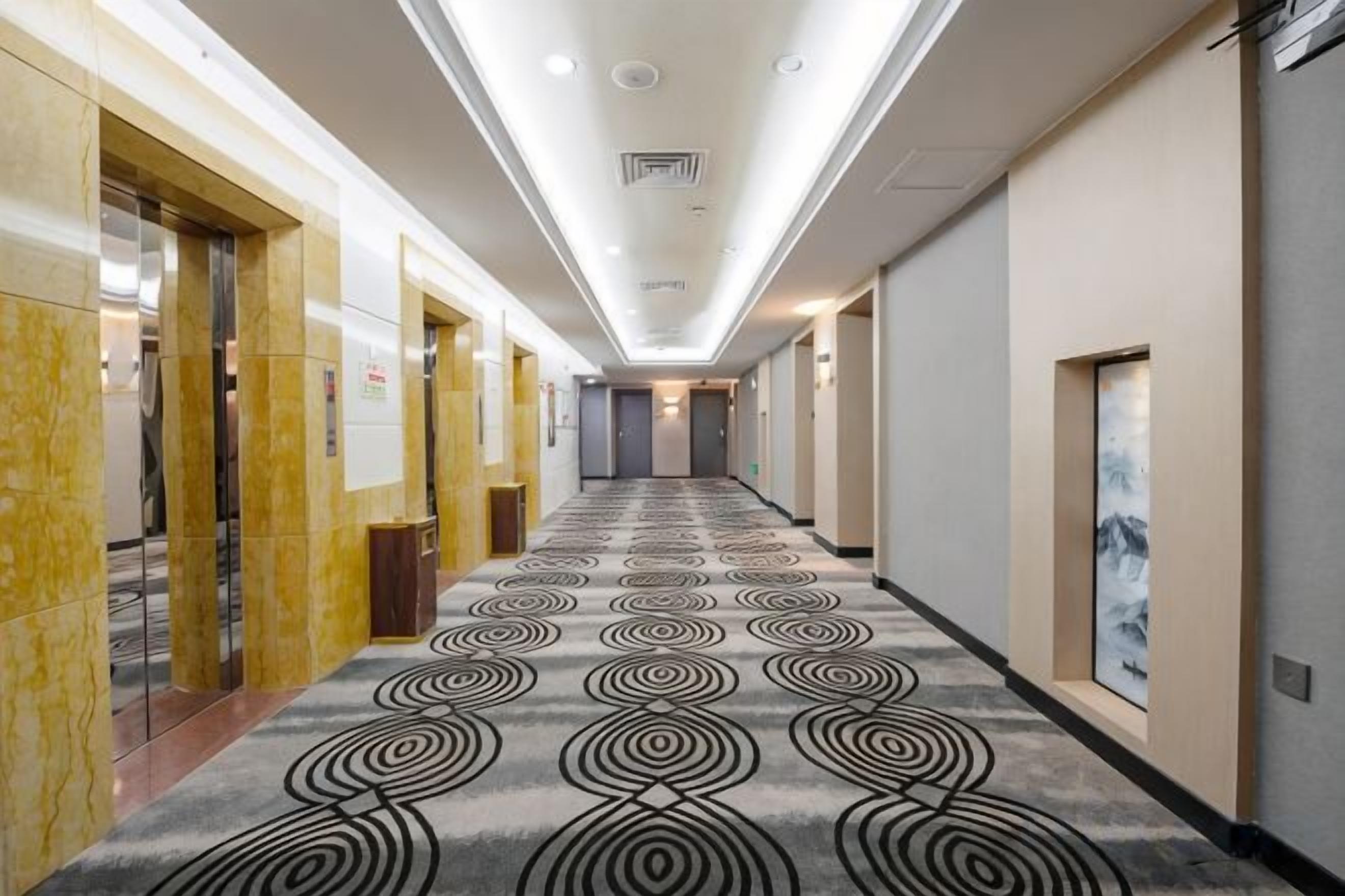 Corredor de hotel com carpete estampado, portas e uma obra de arte emoldurada na parede.
