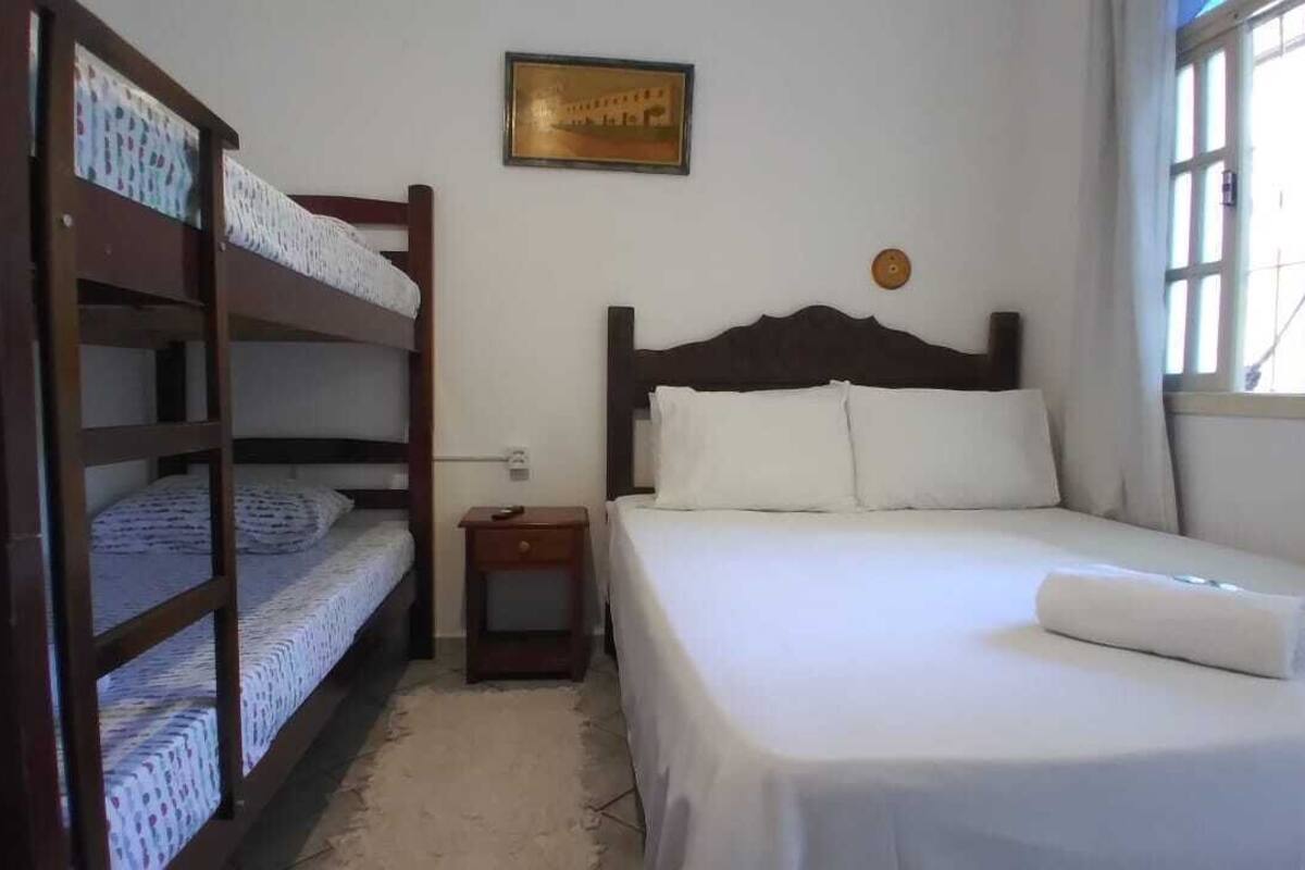 Uma cama de solteiro com cabeceira de madeira, uma mesa de cabeceira e uma cama beliche à esquerda.