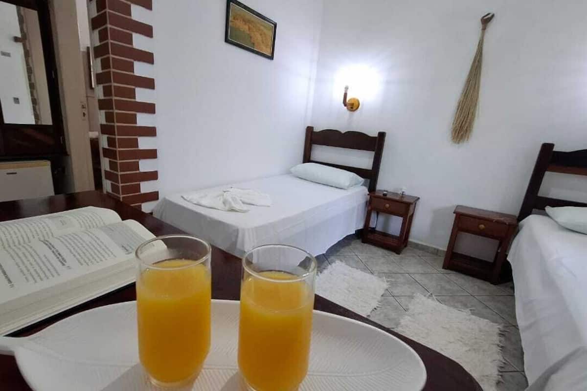 Quarto de hotel com cama, mesas de cabeceira, luminária na parede e uma janela.