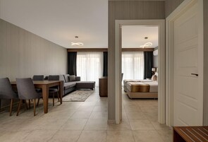 Uma sala moderna com área de jantar, sofá, mesa de centro e vista para um quarto por uma porta aberta.