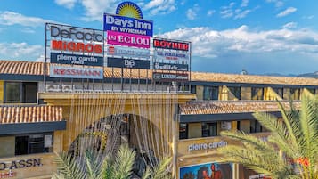 Um hotel com uma grande placa que anuncia várias marcas e comodidades, incluindo Days Inn, Defacto, Migros, ECROU, Boyner e Pierre Cardin.