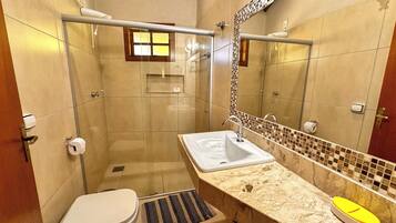 Casa de banho com chuveiro, sanita, lavatório e espelho com painel de mosaicos.