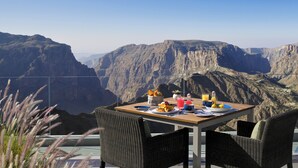 Mesa de jantar com vista para um cânion, cadeiras de vime e uma refeição posta.