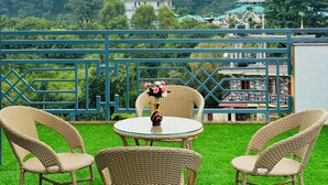 Terraço com cadeiras de vime e uma mesa, com vista para edifícios e árvores.