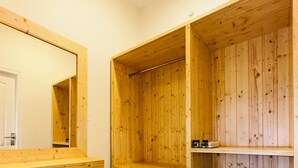 Um quarto de madeira com um banco, um espelho e estantes.