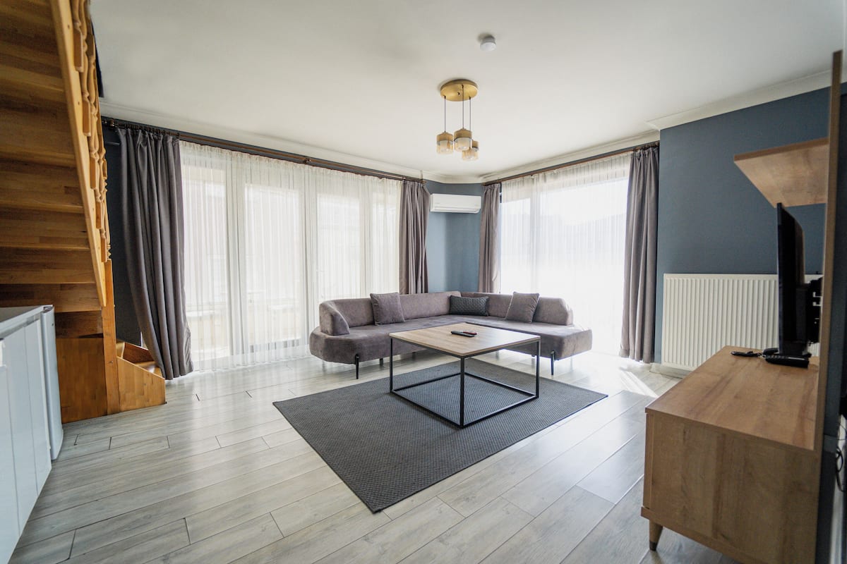 Uma sala de estar moderna com sofá seccional, mesa de centro de madeira e aparador para TV.