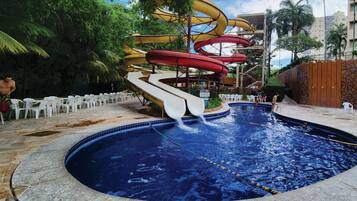 Piscina com vários toboáguas, cercada por palmeiras e um muro de pedra.