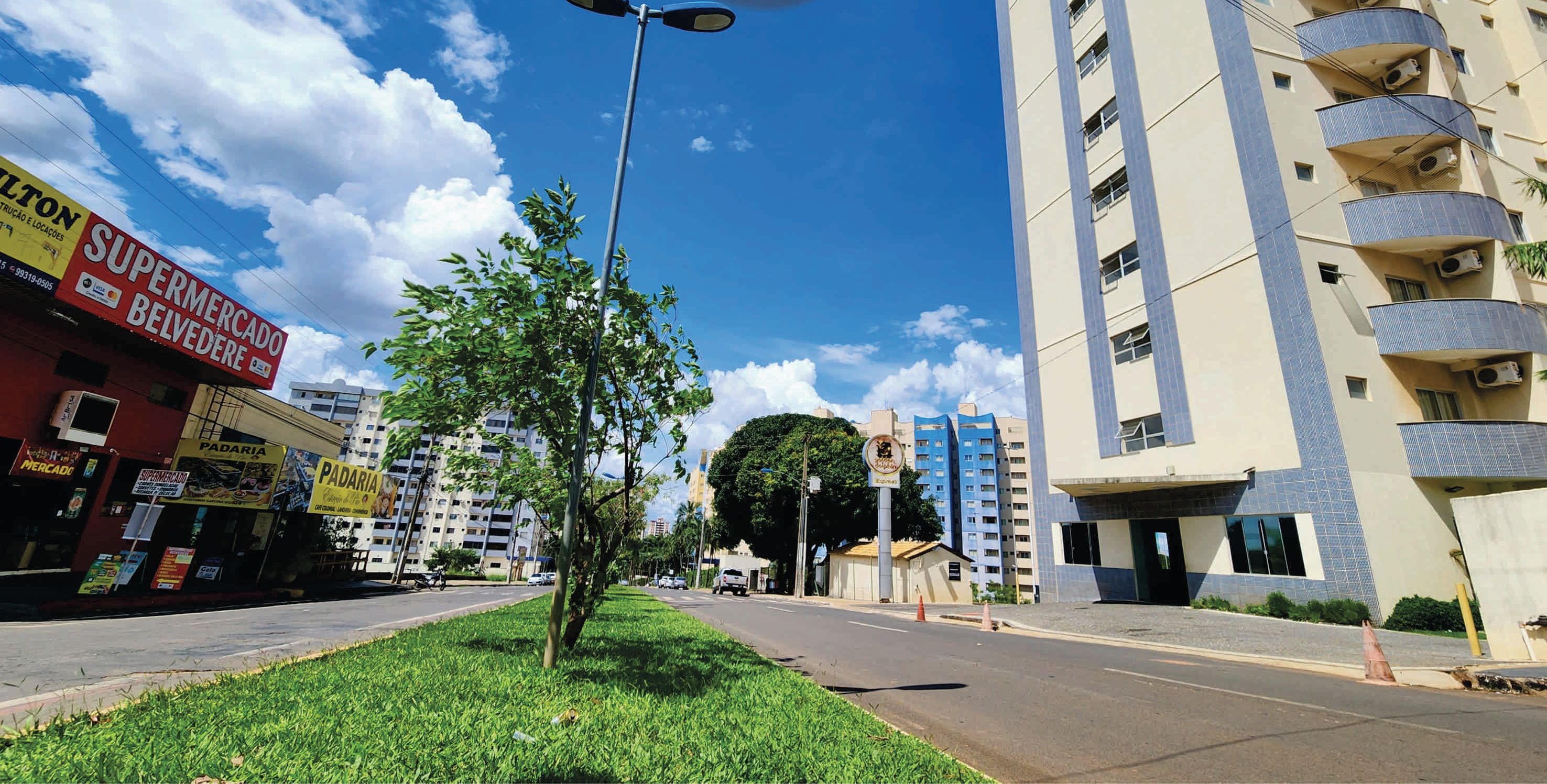 Vista da rua com um edifício com varandas e aparelhos de ar condicionado, um poste de luz e um céu azul límpido.