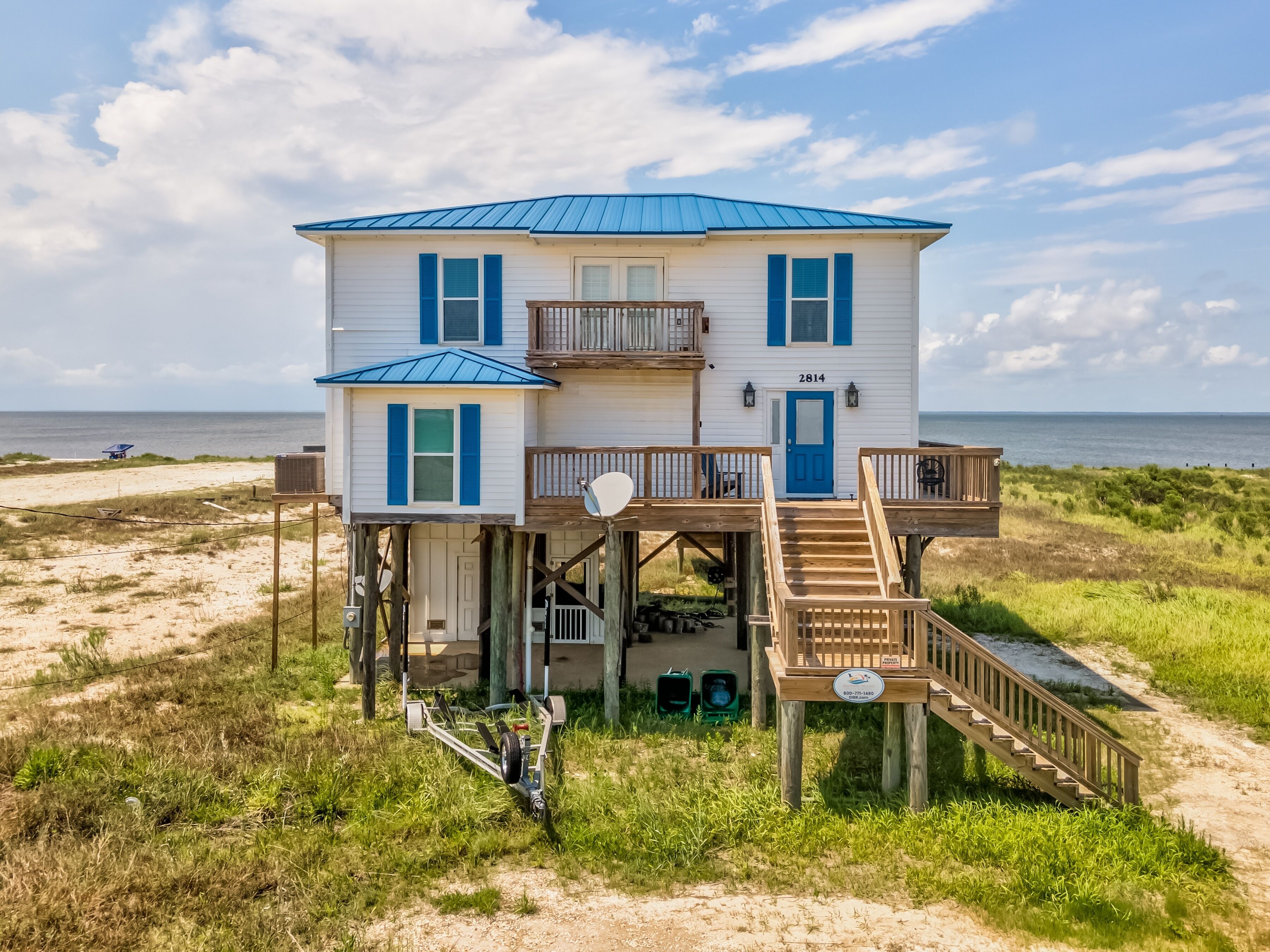 Uma casa de praia de dois andares com telhado azul, varanda e deck com escadas para a entrada.