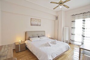 Quarto com cama, mesas de cabeceira, ventilador de teto, um quadro e uma janela com cortinas.