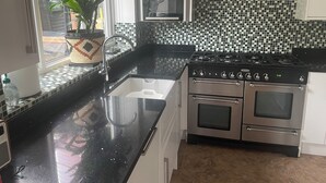 Uma cozinha com bancada preta, eletrodomésticos de aço inoxidável, painel de azulejos e janela com vista para um jardim.