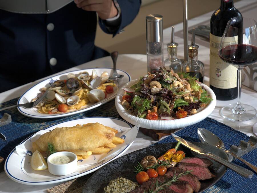 Uma mesa de jantar com diversos pratos, incluindo frutos do mar, salada e bife, juntamente com copos e garrafas de vinho.