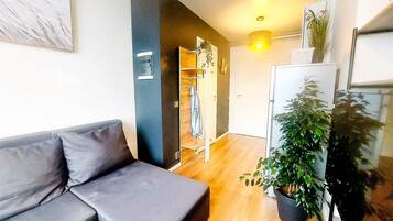 Uma sala de estar moderna com um sofá cinza, piso de madeira, uma planta em vaso e um refrigerador branco.