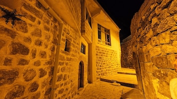 Uma rua estreita com edifícios de pedra, uma porta visível e uma janela com persiana.