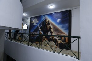 Um corredor com um mural do Esfinge e pirâmides, uma placa com a inscrição 'Egyptian Pyramid' e um corrimão.