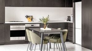 Uma cozinha moderna com armários de madeira escura, bancada branca e uma mesa de jantar com quatro cadeiras.