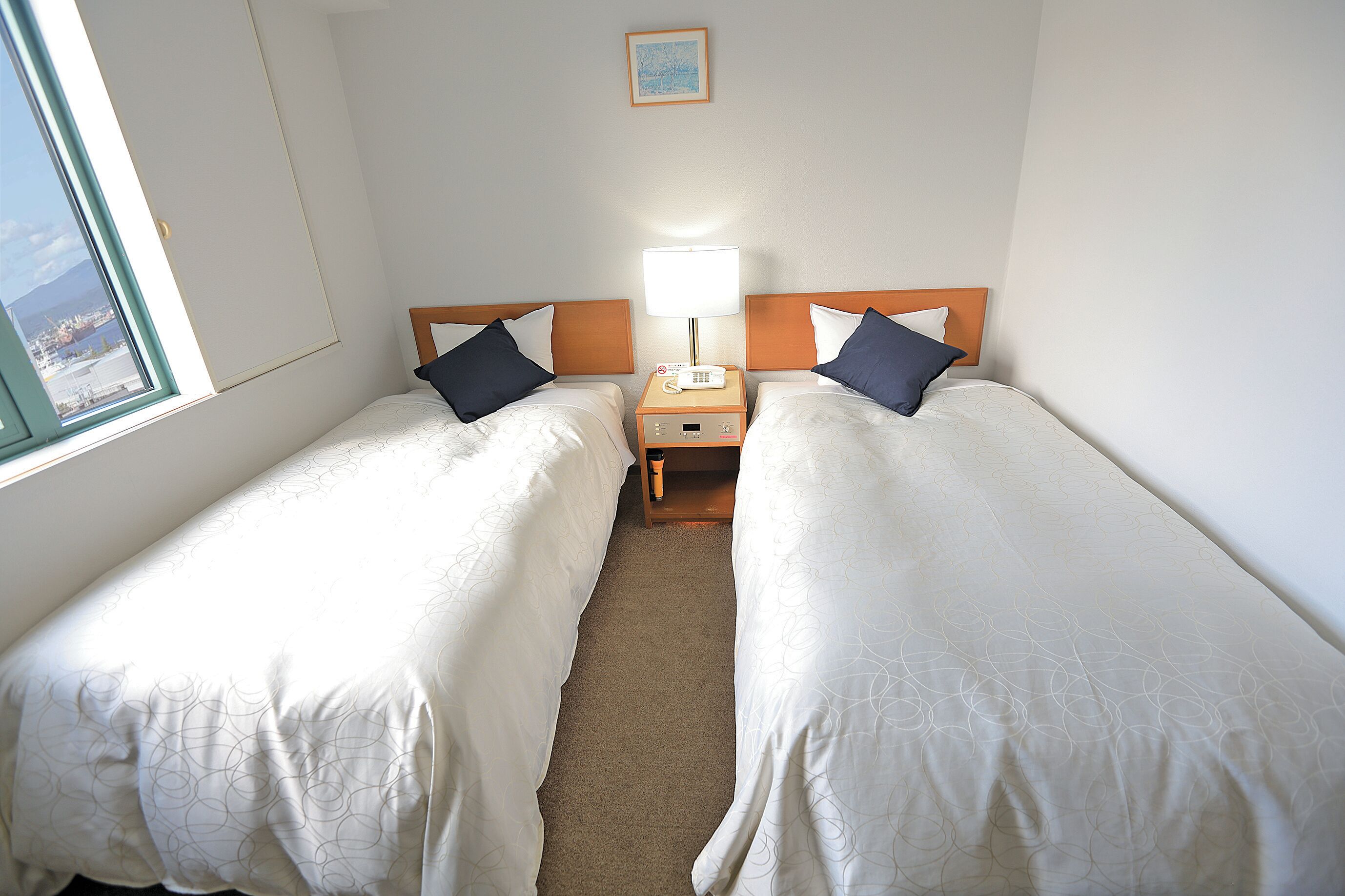 Quarto de hotel com duas camas de solteiro, mesa de cabeceira com abajur e janela com vista para a cidade.
