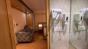 Quarto de hotel com sofá, cama e banheiro com espelho e secadores de cabelo.